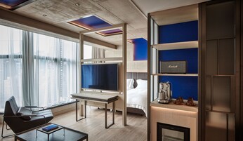 Quarto de hotel moderno com uma janela grande, televisão de tela plana, cama, máquina de café e minibar.