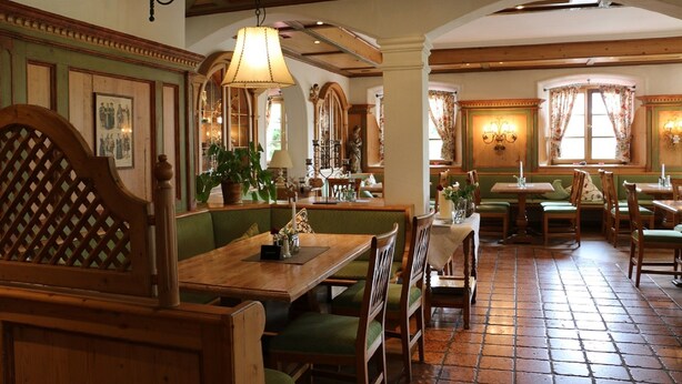 Um restaurante acolhedor com mobiliário de madeira, assentos acolchoados verdes e piso ladrilhado.