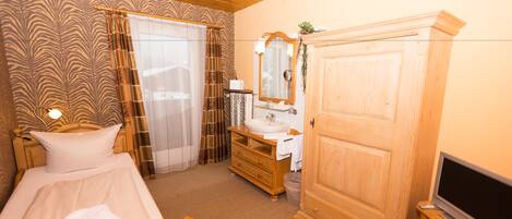 Quarto com cama, guarda-roupa de madeira, penteadeira com espelho e televisão sobre suporte de madeira.