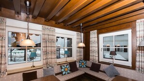 Um quarto acolhedor com teto de madeira, um sofá com almofadas florais e duas janelas com cortinas.