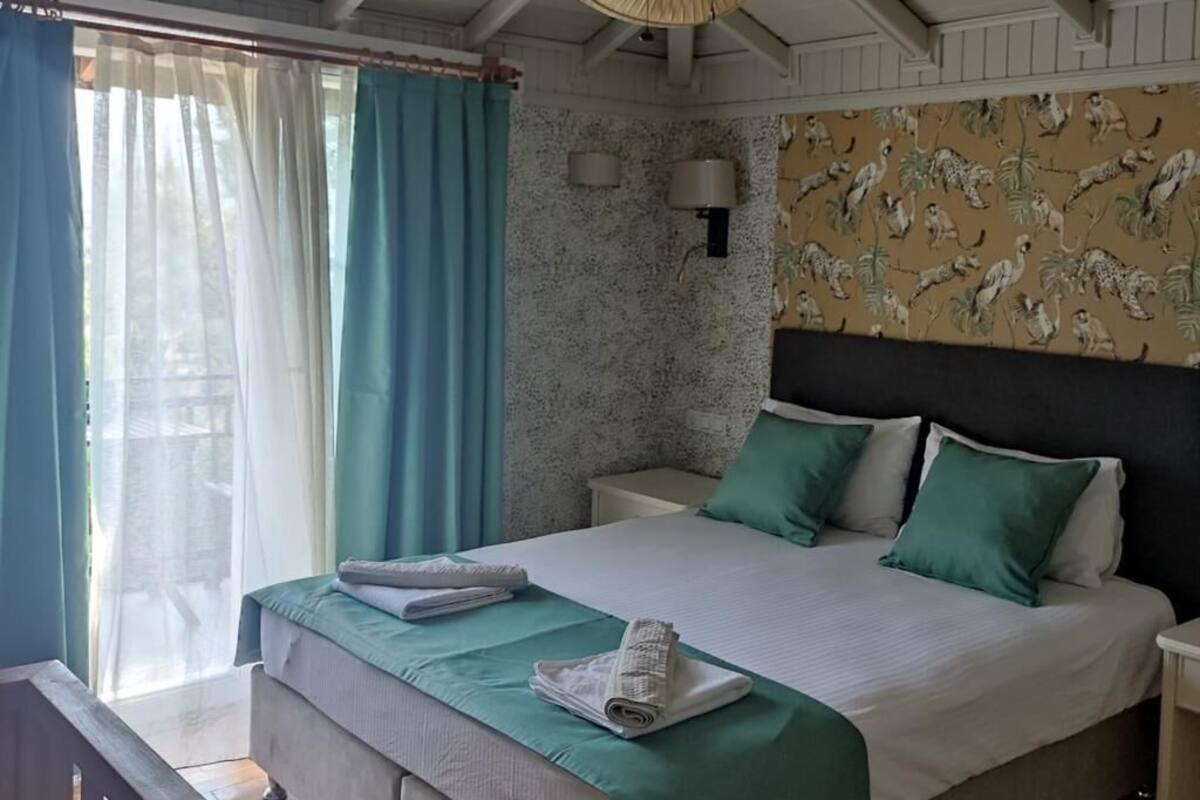 Quarto de hotel com cama, ventoinha no teto, mesa de cabeceira e janela com cortinas.