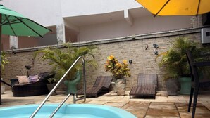 Piscina com escada de metal, espreguiçadeiras, plantas em vasos e guarda-sóis.