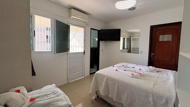 Quarto de hotel com cama, televisão, espelho, porta e janela.