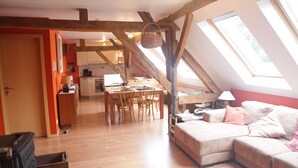 Um amplo loft com pé direito alto, vigas de madeira aparente, área de jantar e um espaço de estar aconchegante com sofá e almofadas.
