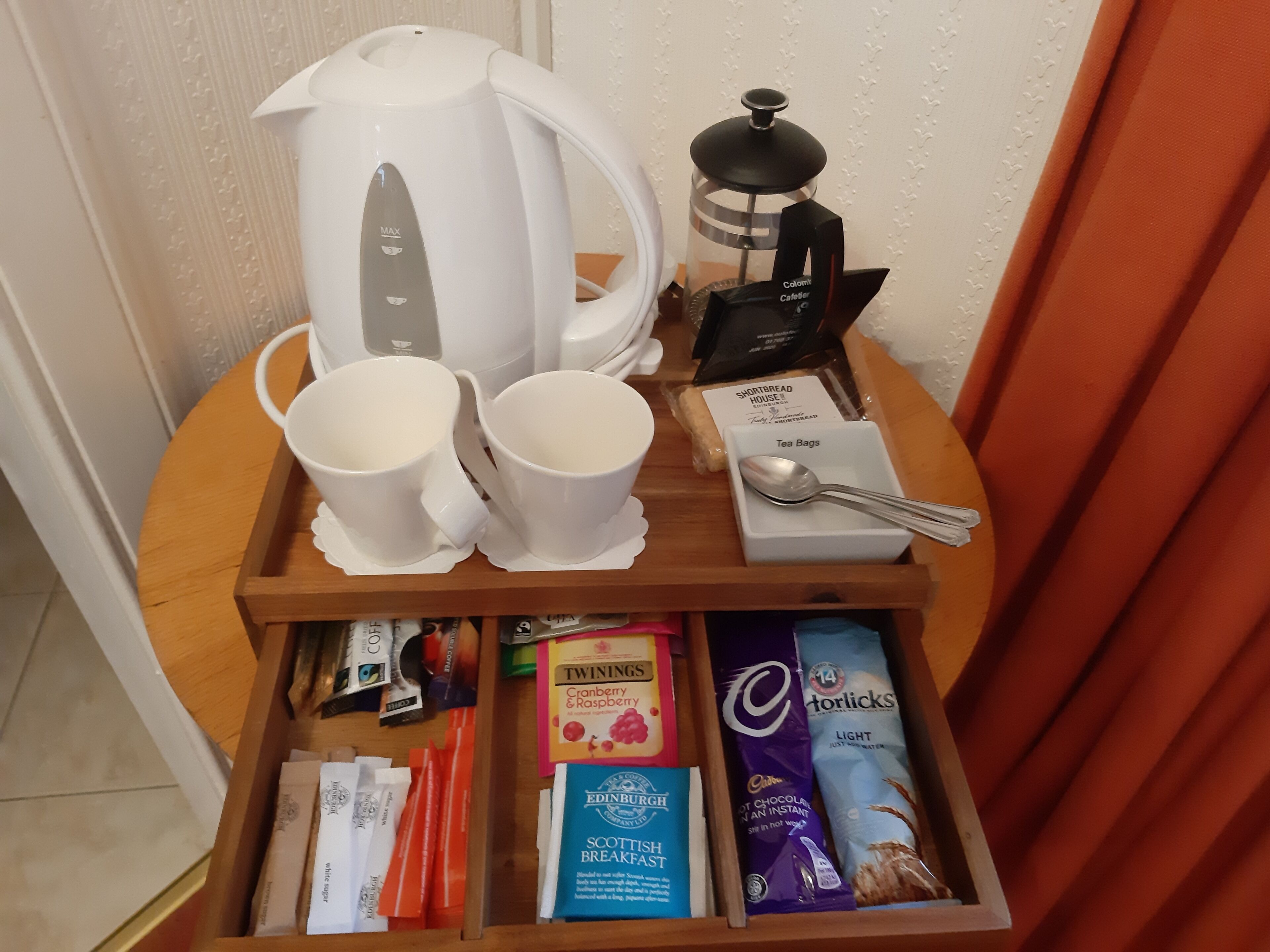 Uma bandeja de café da manhã com duas xícaras brancas, uma colher e uma cafeteira.