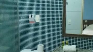 Uma casa de banho com sanita, um pequeno contentor de lixo e lavatório com espelho em cima.