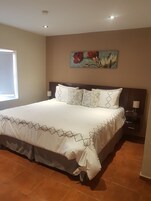 Um quarto com uma cama grande, uma mesa de cabeceira, uma luminária, um quadro na parede e uma janela.