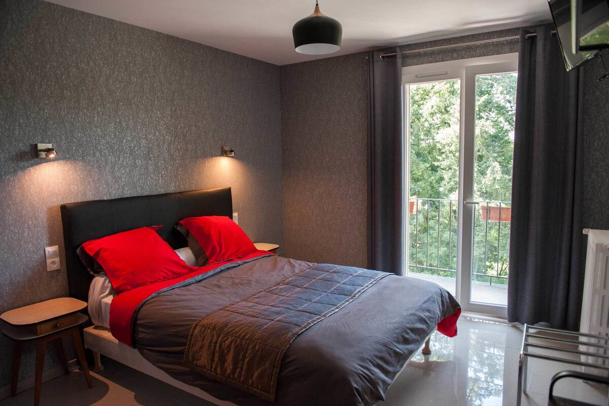 Quarto moderno com uma cama grande, duas mesas de cabeceira, uma luminária no teto e vista para o exterior através de uma porta de vidro deslizante.