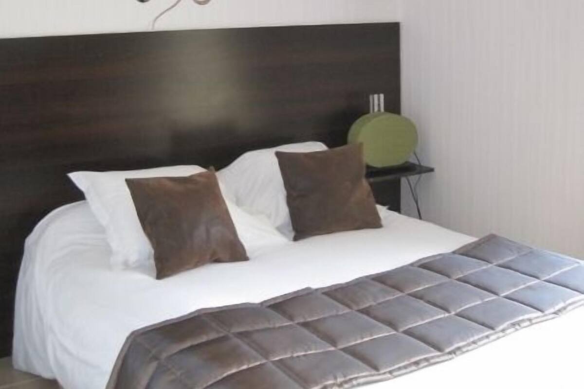 Cama bem arrumada com colcha marrom e duas almofadas, cabeceira de madeira escura e decoração na parede com padrões circulares.