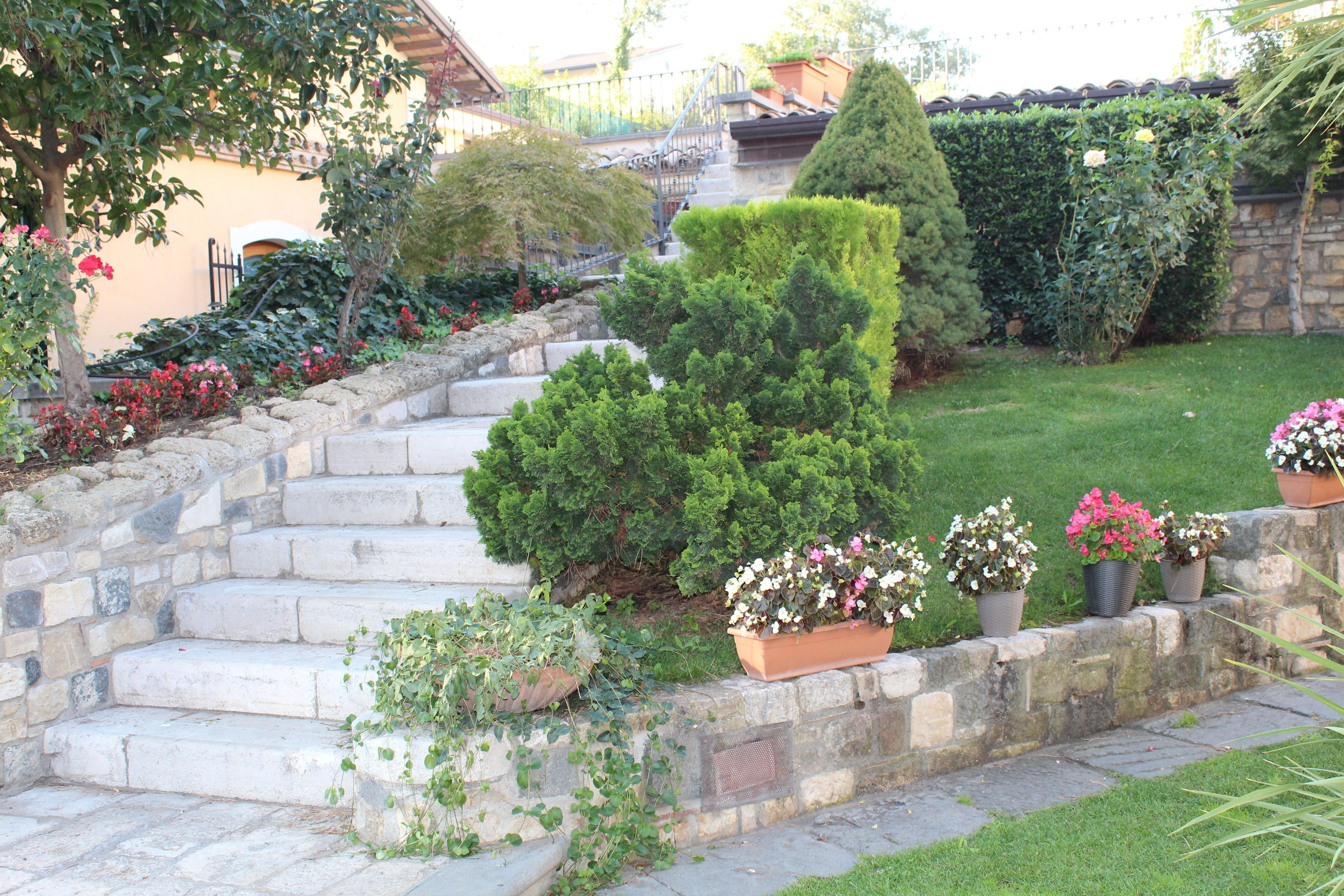 Escadaria de pedra levando a uma casa com um jardim bem cuidado, incluindo vasos de plantas e um sebe.