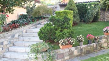 Escadaria de pedra levando a uma casa com um jardim bem cuidado, incluindo vasos de plantas e um sebe.