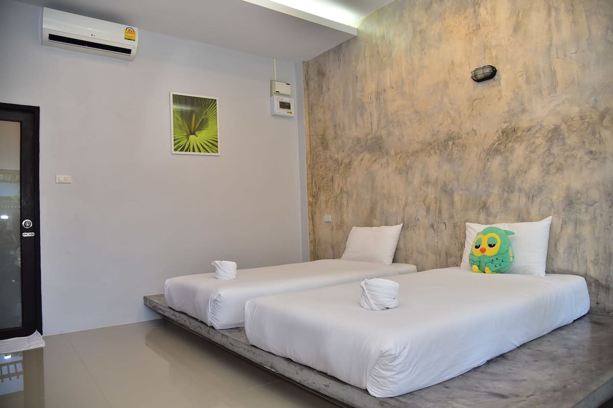 Quarto de hotel com duas camas, um pedestal de mármore, um aparelho de ar condicionado, uma luminária fixada na parede e um pequeno dispositivo também fixado na parede.