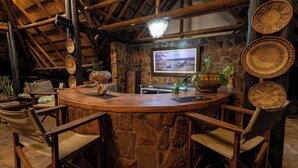 Um espaço de bar rústico, com paredes de pedra, cadeiras de madeira e uma tela de televisão.