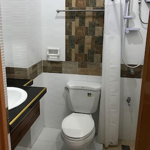Casa de banho com sanita branca, lavatório com bancada preta e área de duche com parede em azulejos.