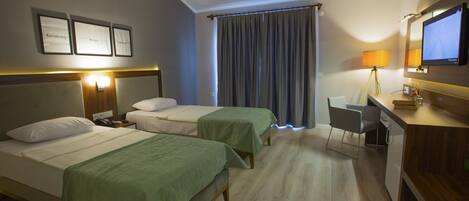 Quarto de hotel com duas camas, uma mesa com cadeira, televisão e janela com cortinas.