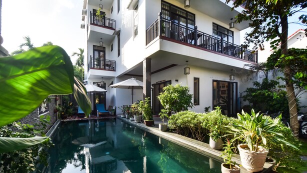 Piscina com vasos de plantas e um edifício de dois andares com sacadas.