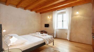 Quarto com teto de madeira, cama com roupa branca, abajur e janela com cortinas.