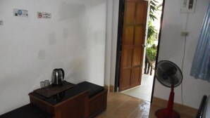 Quarto pequeno com um armário de madeira, chaleira e ventilador.
