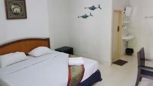 Quarto de hotel com cama, mesa de cabeceira, cadeira, prateleira na parede e porta para o banheiro.