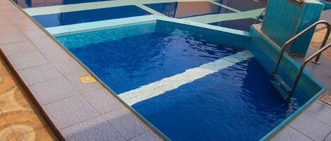 Uma piscina com água azul cristalina, bordas e piso azulejados.
