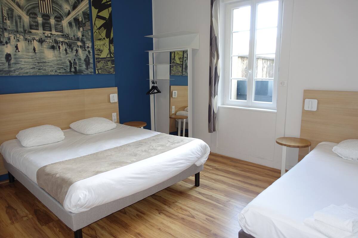 Quarto de hotel com uma cama grande, uma cama menor, um espelho, uma janela e um quadro na parede.