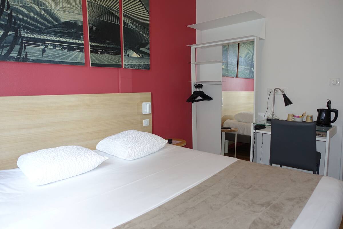 Quarto de hotel com cama, escrivaninha, cadeira e espelho.