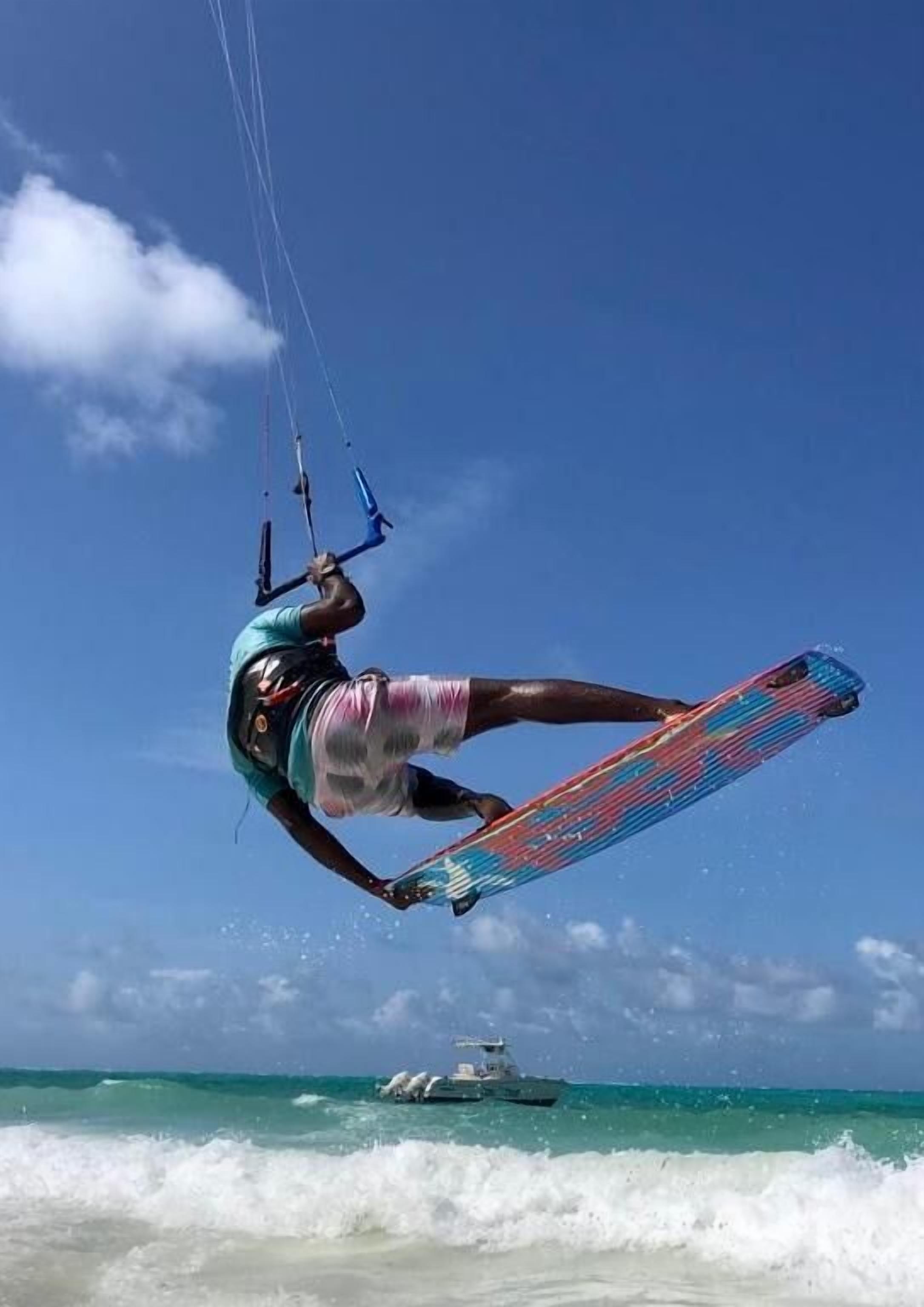 Uma pessoa praticando kitesurf sobre águas azul-turquesa, com um barco ao fundo.