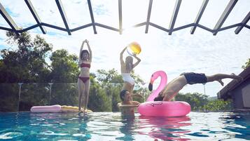 Piscina com pessoas brincando, um flutuador em forma de flamingo rosa e céu claro.