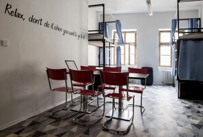 Um dormitório com beliches, uma mesa de jantar com cadeiras e uma frase motivacional na parede.