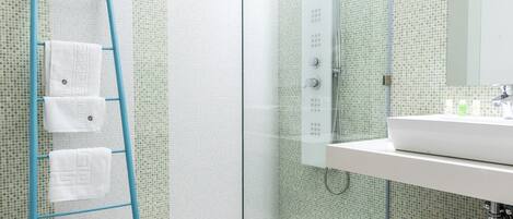 Uma casa de banho moderna com cabine de duche em vidro, lavatório branco e toalheiro com várias toalhas.