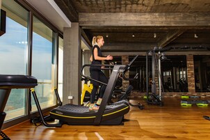 Uma academia com esteira, equipamentos de ginástica e grandes janelas com vista para a água.