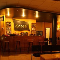 Uma área de bar com uma placa que diz "Roots" e vários bancos e mesas.