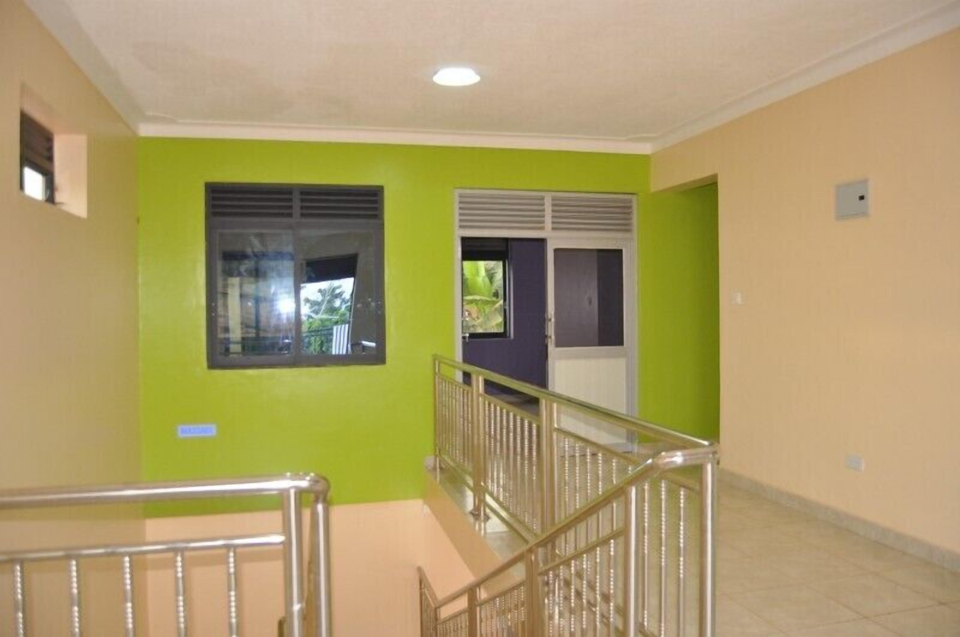 Um corredor com parede verde, janela com persianas, porta e corrimão de metal.