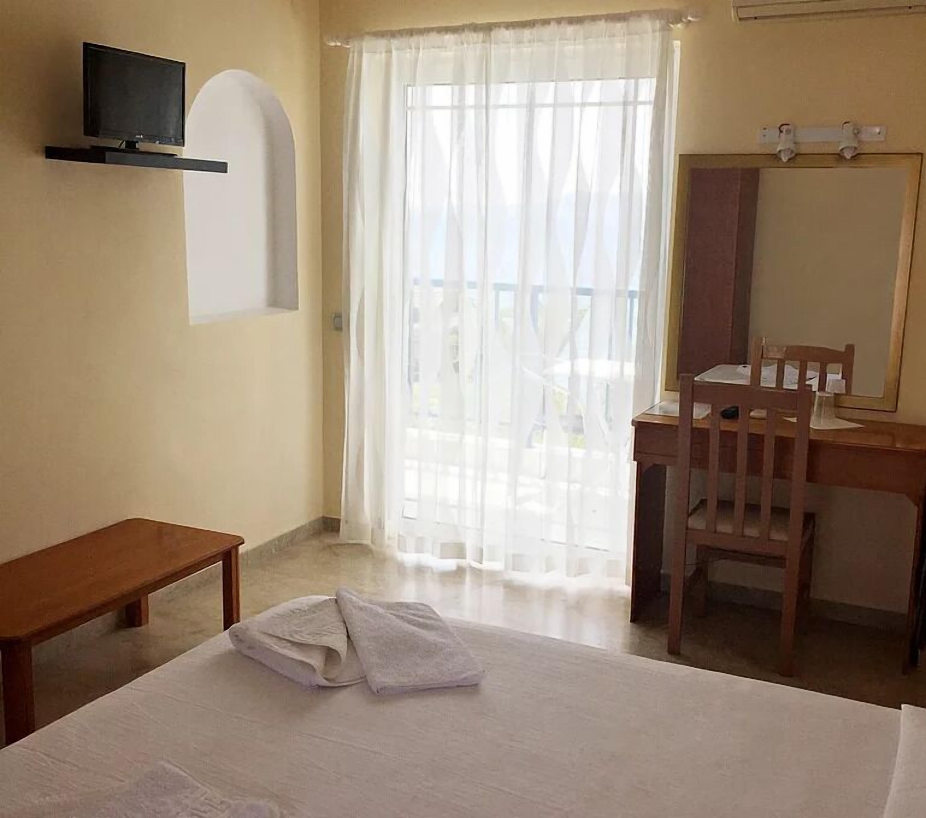 Quarto de hotel com cama, escrivaninha, cadeira, televisão fixada na parede e varanda com vista.