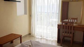 Quarto de hotel com cama, escrivaninha, cadeira, televisão fixada na parede e varanda com vista.