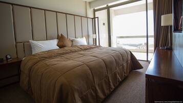 Quarto de hotel com cama grande, mesa de cabeceira, escrivaninha e vista para a cidade pela janela.