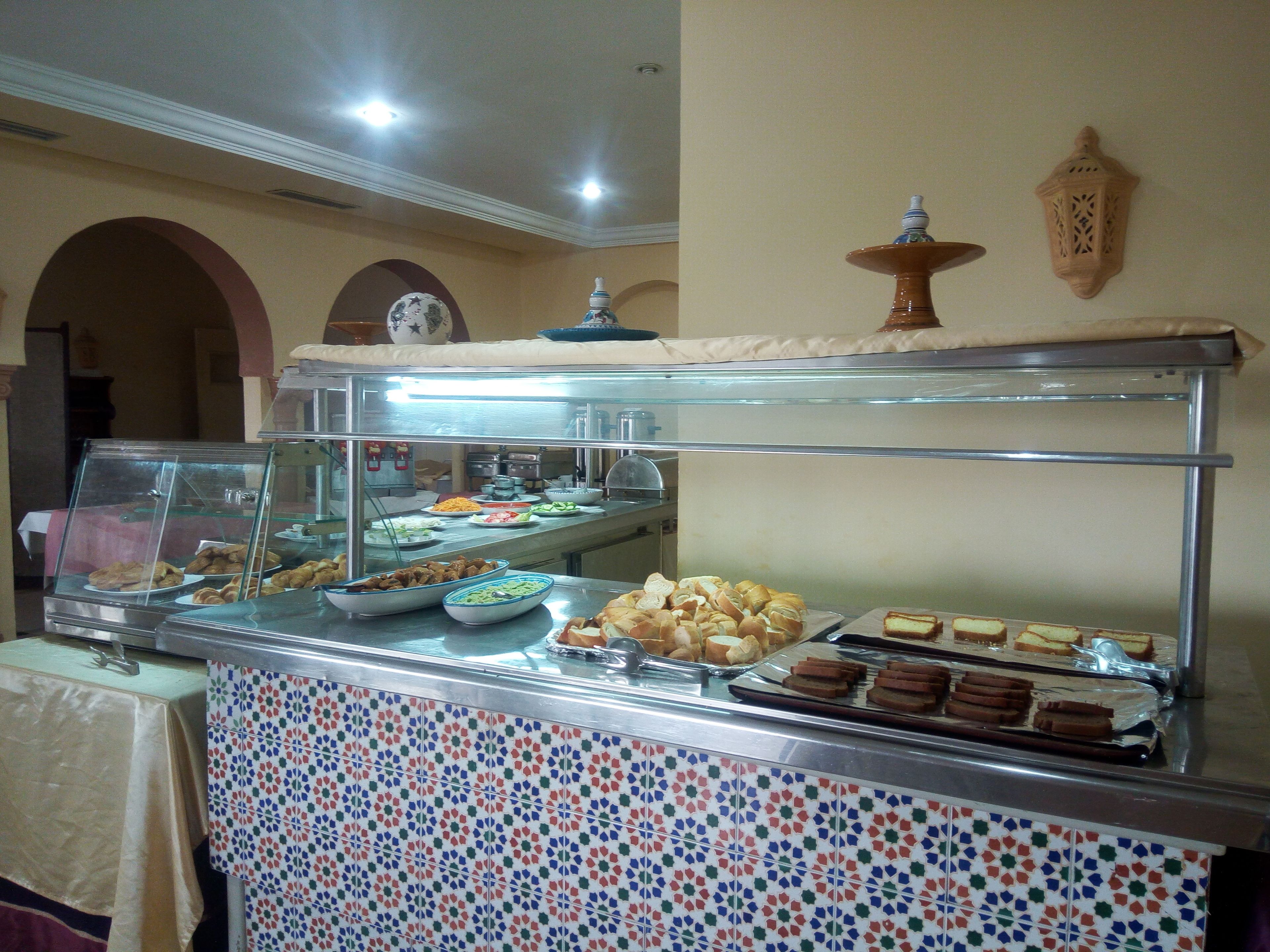 Buffet com diversos alimentos, toalha de mesa estampada e parede decorativa.