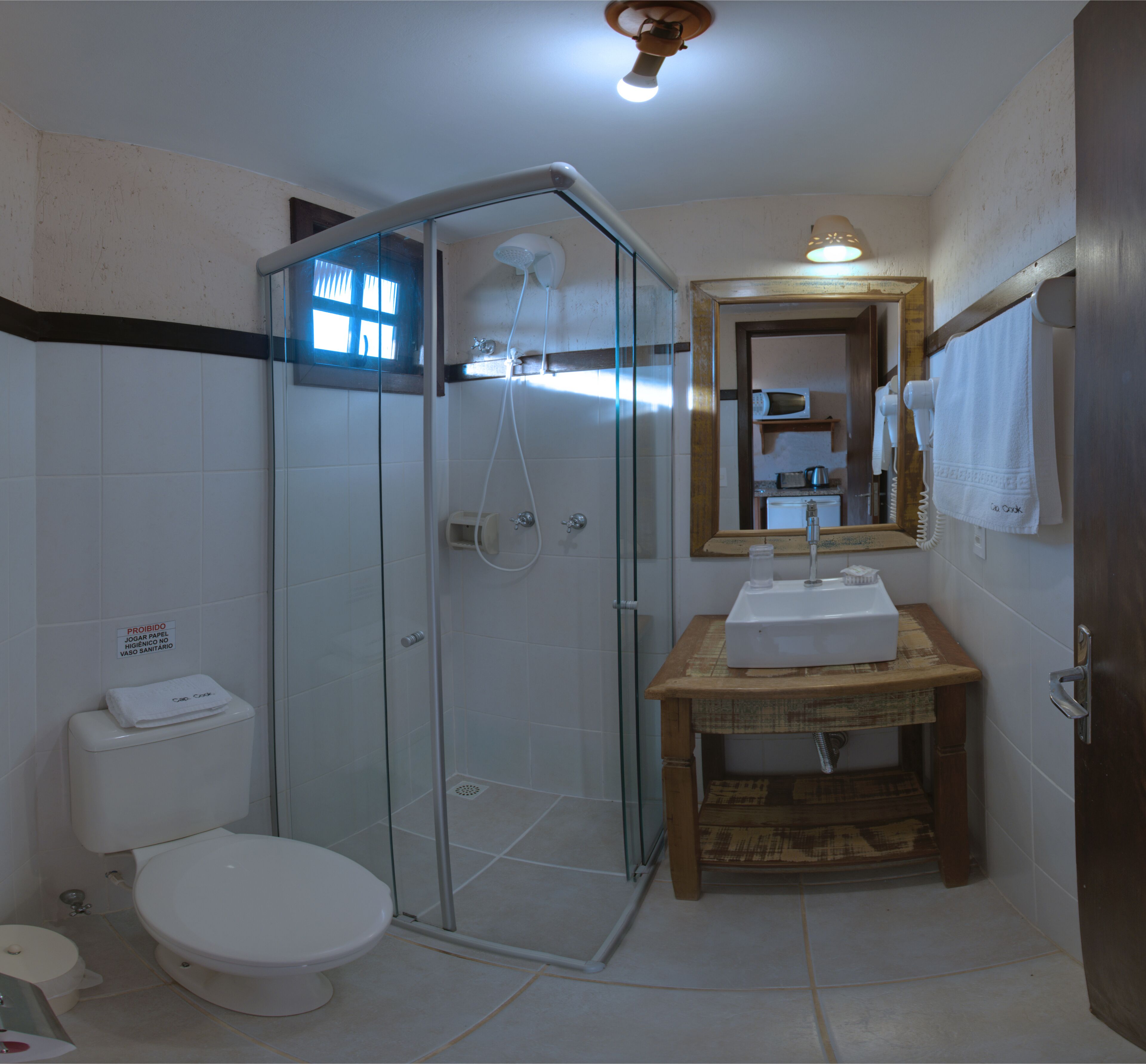 Casa de banho com chuveiro em cabine de vidro, sanita e lavatório com bancada de madeira.