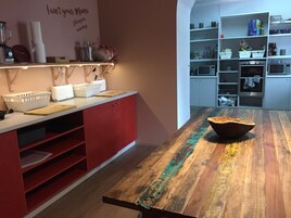 Uma cozinha com mesa de madeira, armários vermelhos e uma prateleira na parede com utensílios de cozinha.
