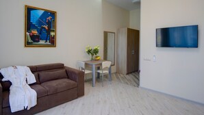 Uma sala de estar moderna com um sofá marrom, uma mesa de jantar com duas cadeiras, um quadro e uma televisão de tela plana na parede.