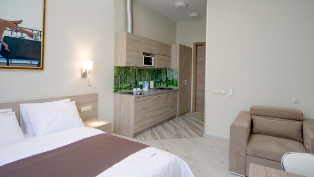 Quarto de hotel com cama, sofá, cozinha compacta e um quadro na parede.