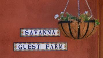 Placa com a inscrição 'SAVANNA GUEST FARM' e um vaso pendurado acima.