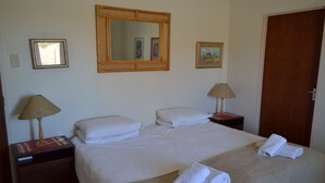 Quarto de hotel com uma cama grande, duas mesas de cabeceira com luminárias, um espelho e uma porta.