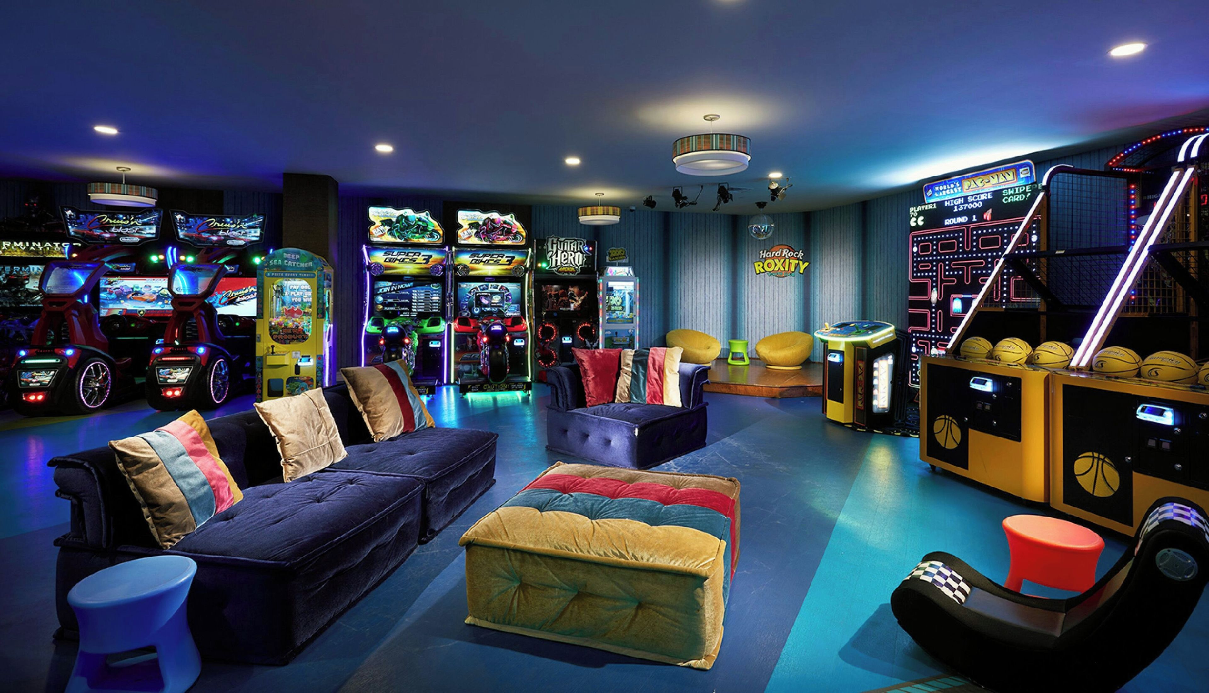 Quarto com sofá, pufê e jogos de fliperama.