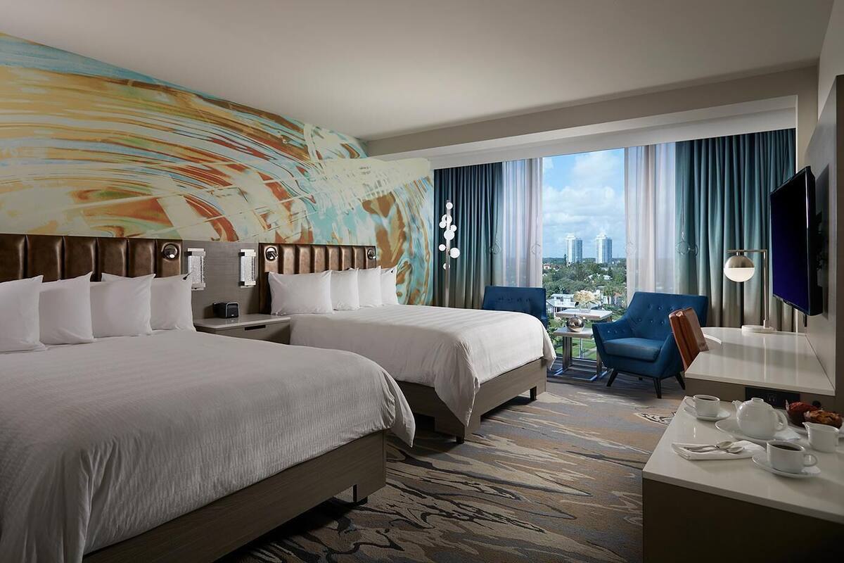 Quarto de hotel com duas camas, televisão, secretária com cadeira e vista para a cidade.