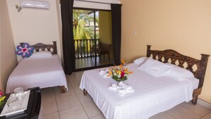 Quarto de hotel com duas camas, uma varanda e vista para palmeiras, além de uma mesinha com bandeja.