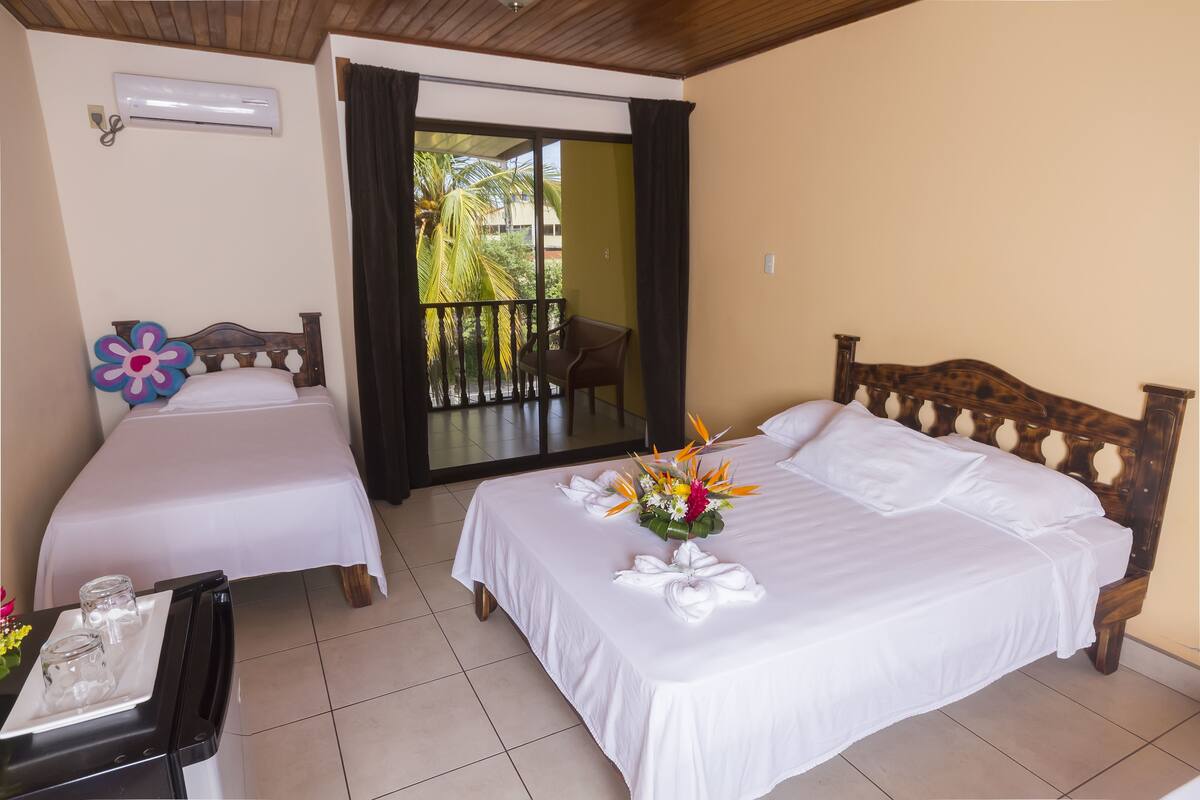 Quarto de hotel com duas camas, uma varanda e vista para palmeiras, além de uma mesinha com bandeja.
