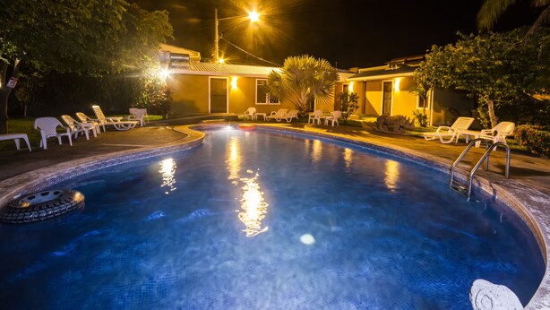 Piscina com espreguiçadeiras e um edifício ao fundo.