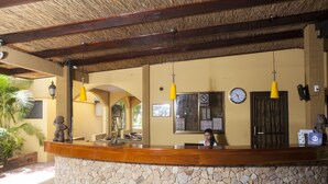 Uma área de recepção com balcão de pedra, vigas de madeira e luminárias pendentes amarelas.