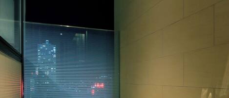 Casa de banho moderna com uma banheira grande, divisória de vidro e vista para a cidade à noite.